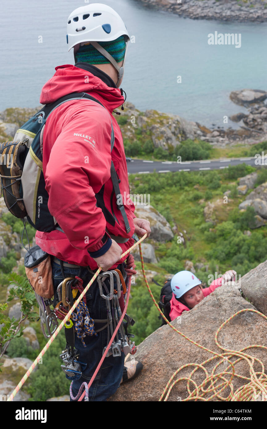 A male climber belaying a female climber as she climbs up a granite ...