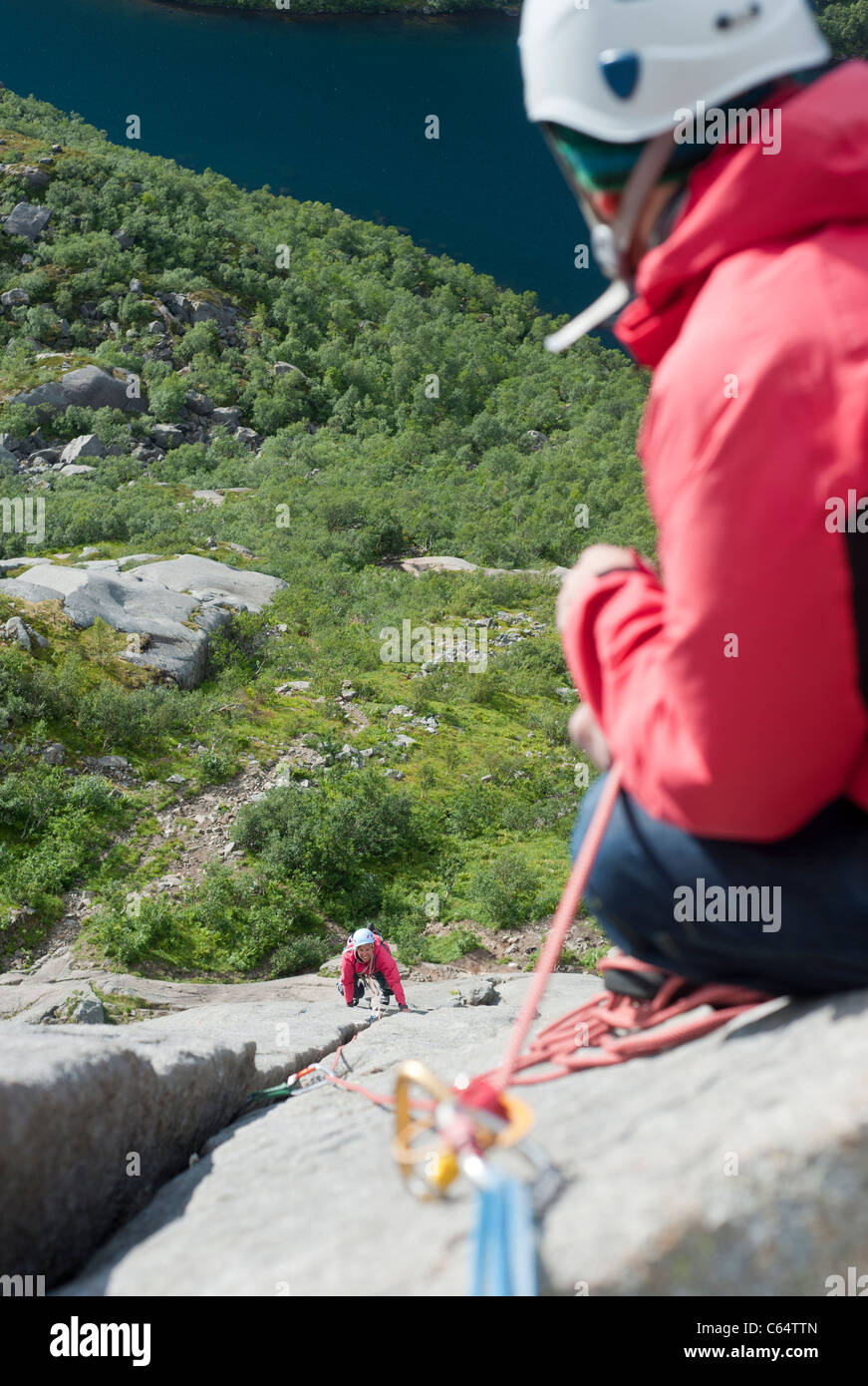 A male climber belaying a female climber as she climbs up a granite ...