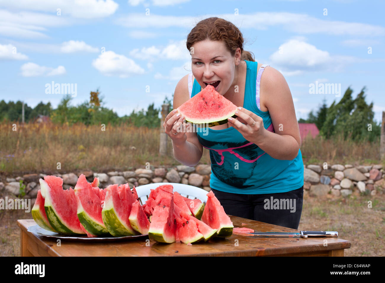 Young Russian woman eating watermelon. Many red slices on table ...