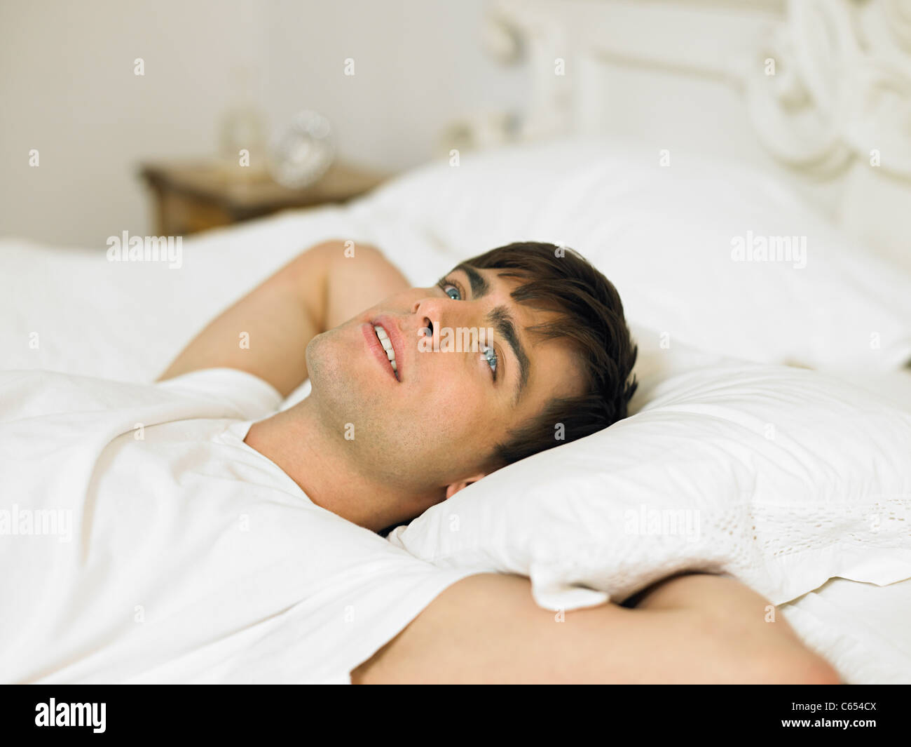 Young man lying on bed with hands behind head Stock Photo - Alamy