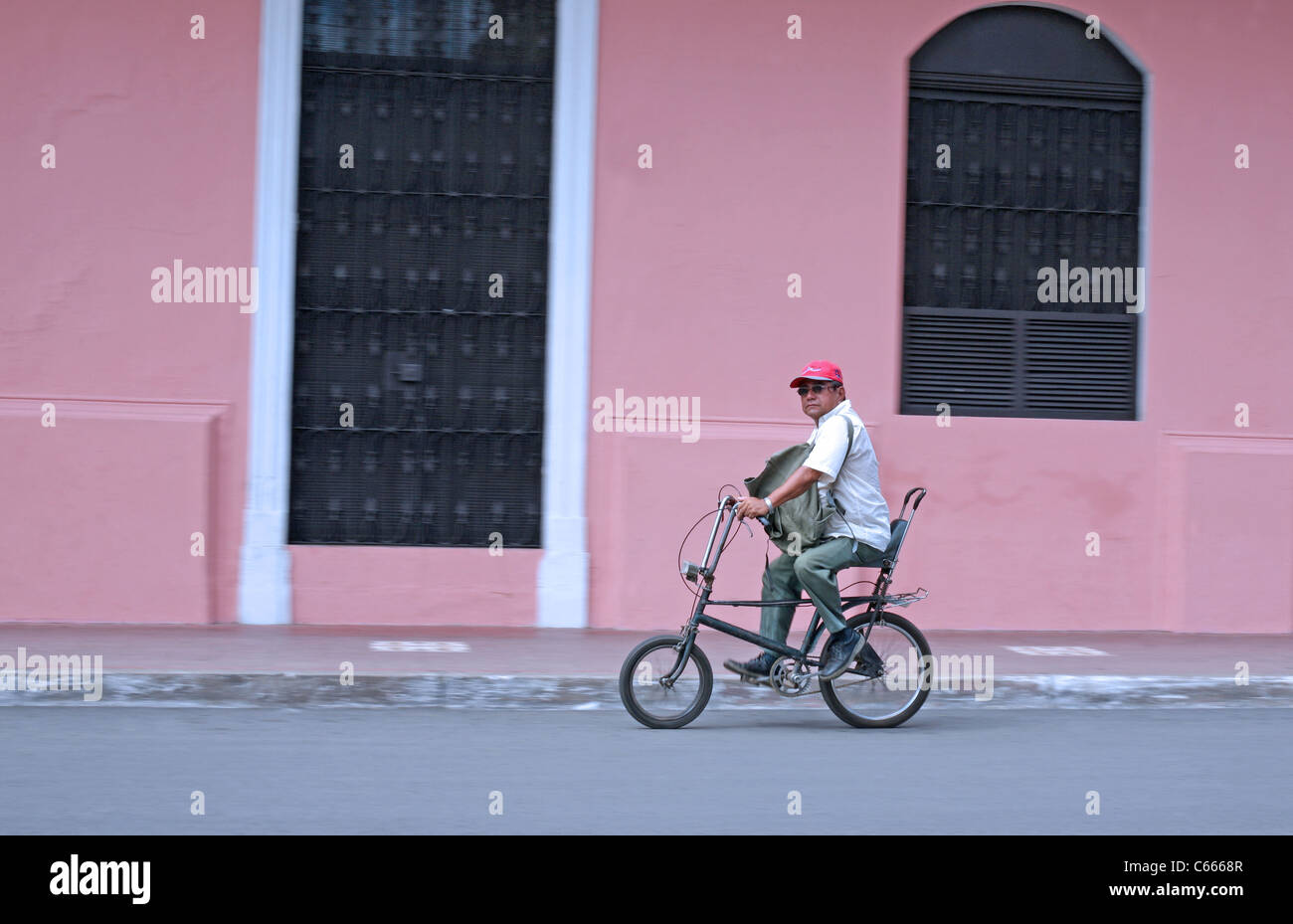 Man on small bicycle riding past pink building Stock Photo - Alamy