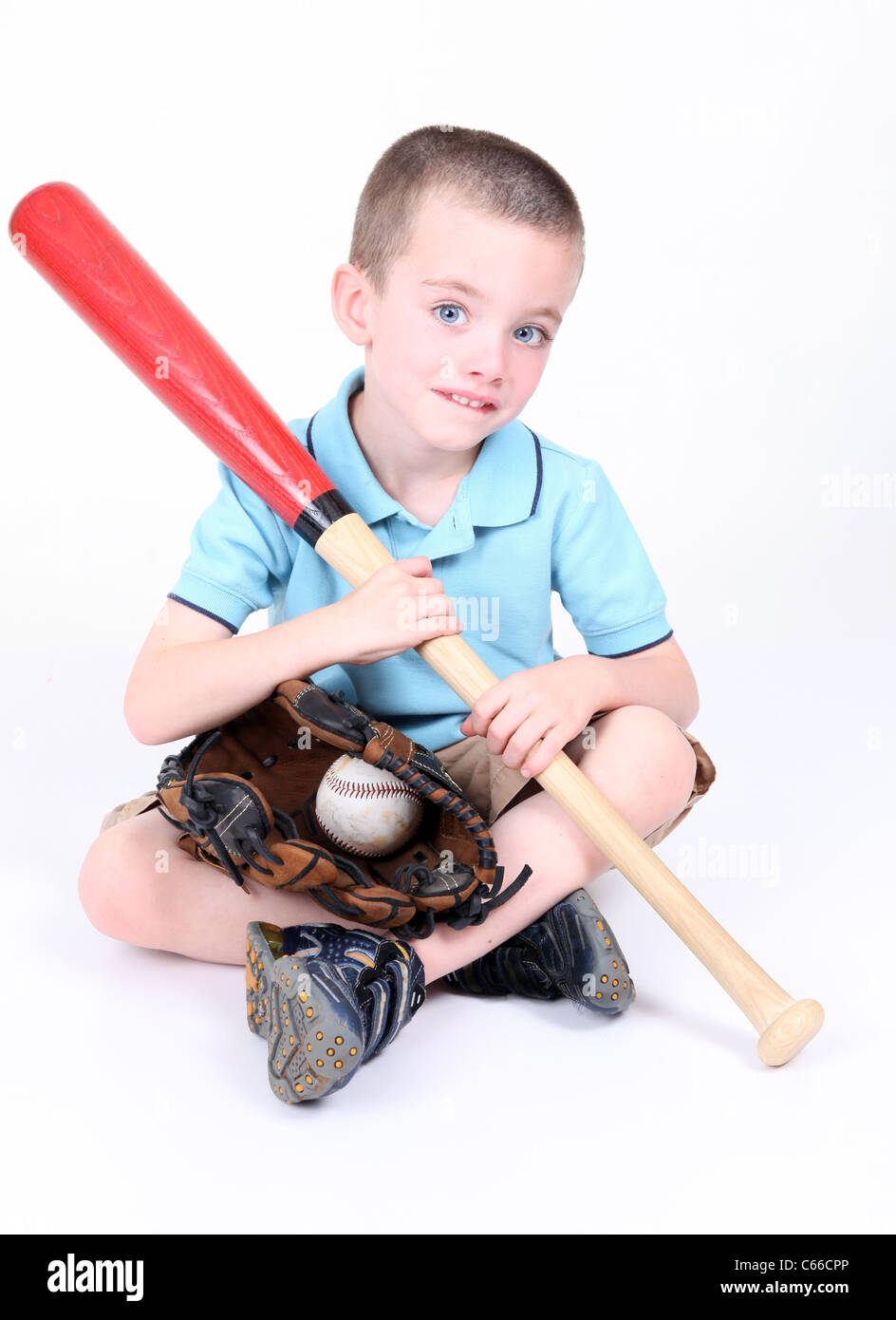 Young boy biting his lip holding a baseball bat with ball and glove ...