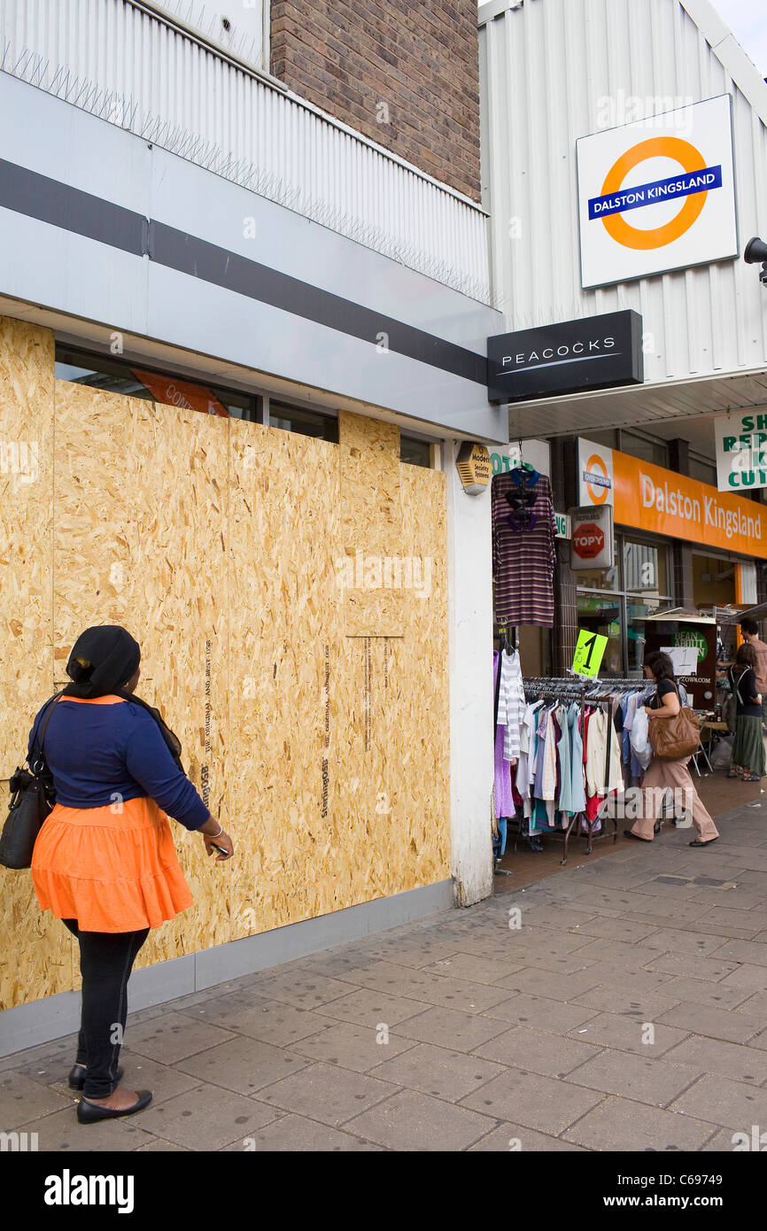 A woman walks past a boarded up shop damaged in the London riots of ...