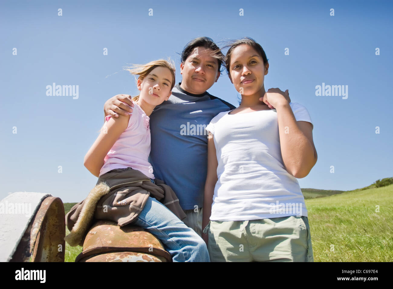 A multi ethnic family, hugging and bonding in a field of grass during a ...