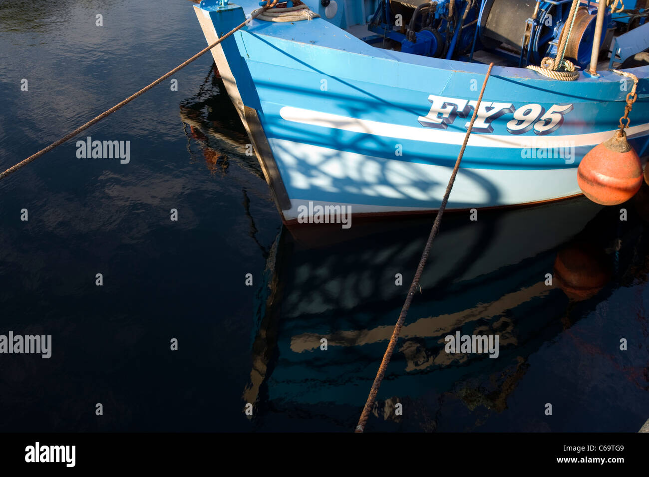The blue and white hull of FY95 fishing boat reflected in the water at ...