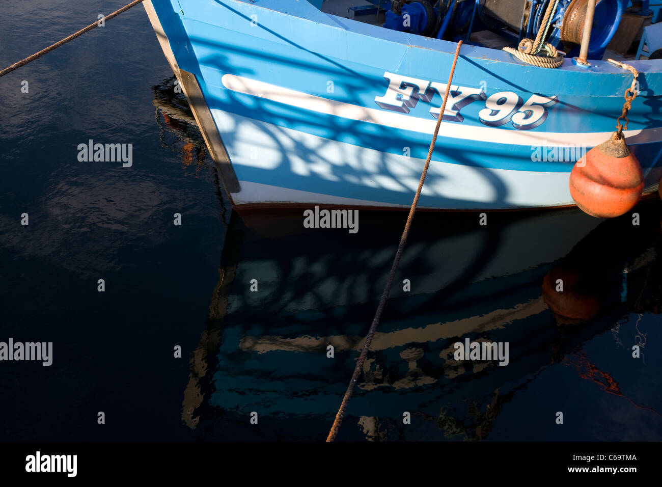The blue and white hull of FY95 fishing boat reflected in the water at ...