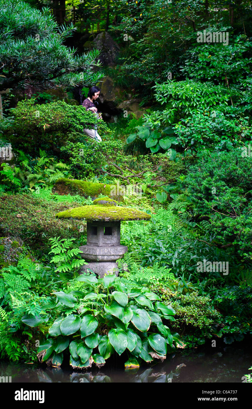 Tranquil Japanese garden with stone lantern. A woman is walking in the ...