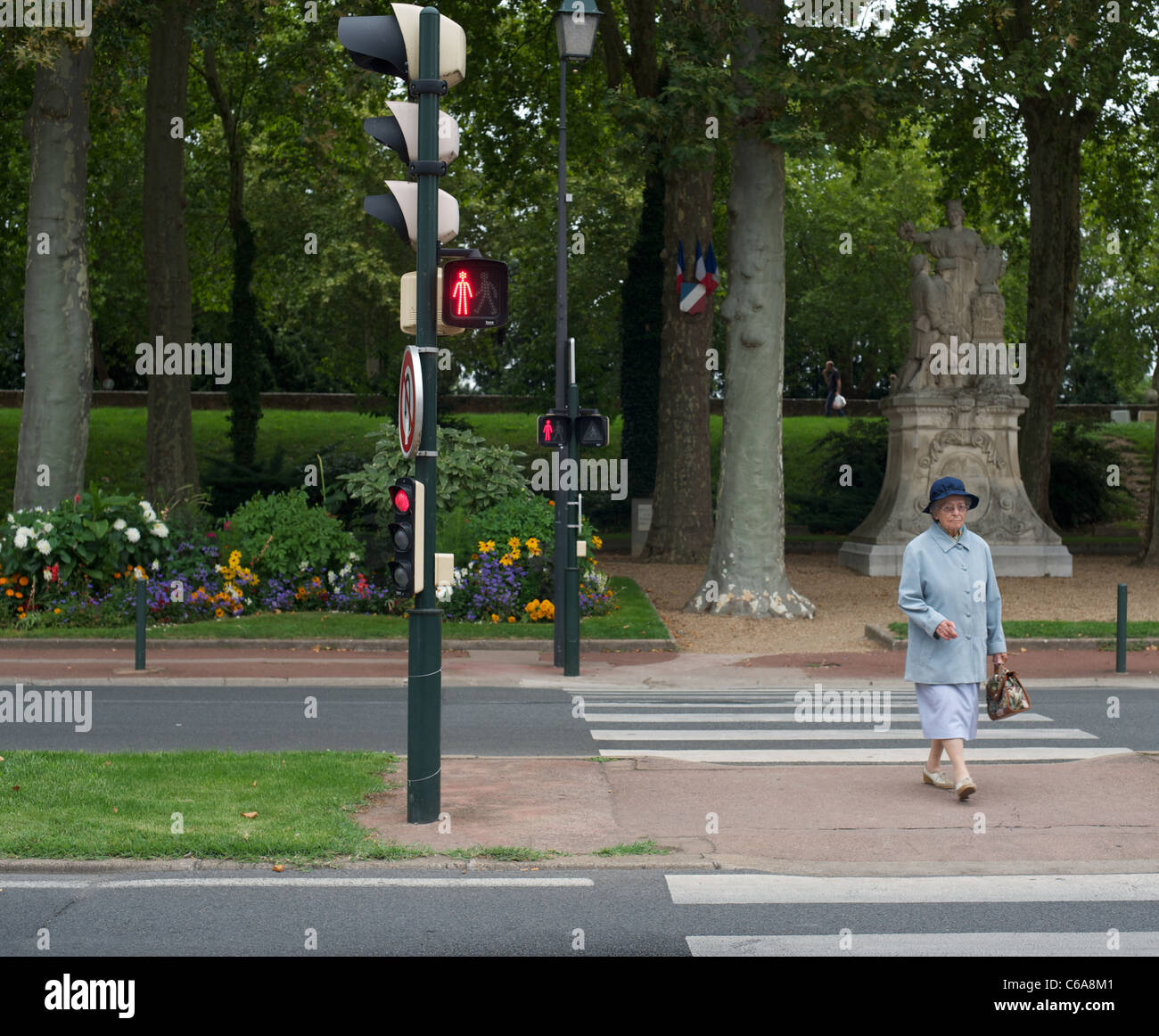 A smartly dressed lady crossing a pedestrian crossing near a park in ...