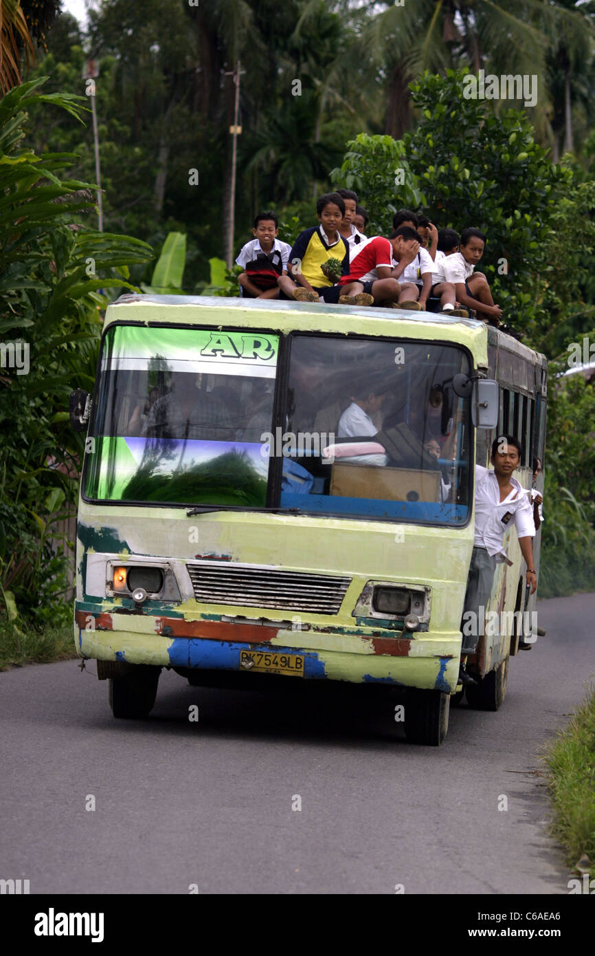 Children ride on the roof of a bus on their way to school. Bukit Lawang ...