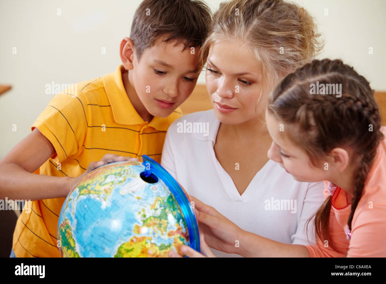 Portrait of cute classmates and teacher looking at globe at geography ...