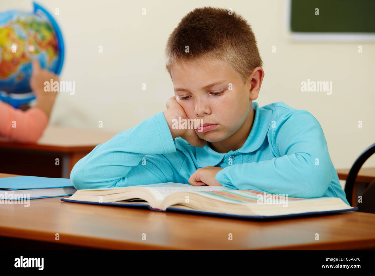 Cute schoolboy reading book in class during lesson Stock Photo - Alamy