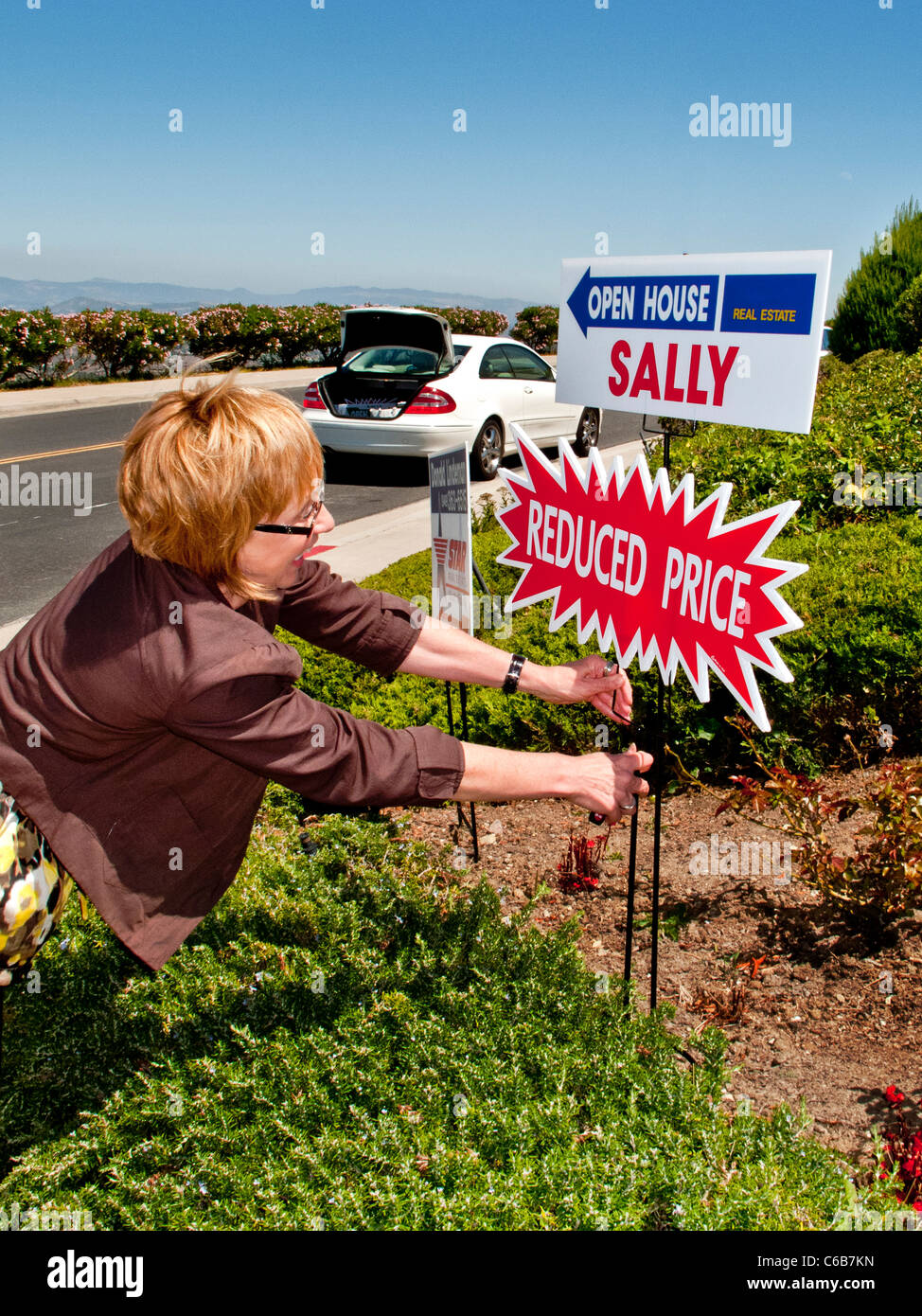 A woman realtor posts temporary signs pointing the way to her "open ...