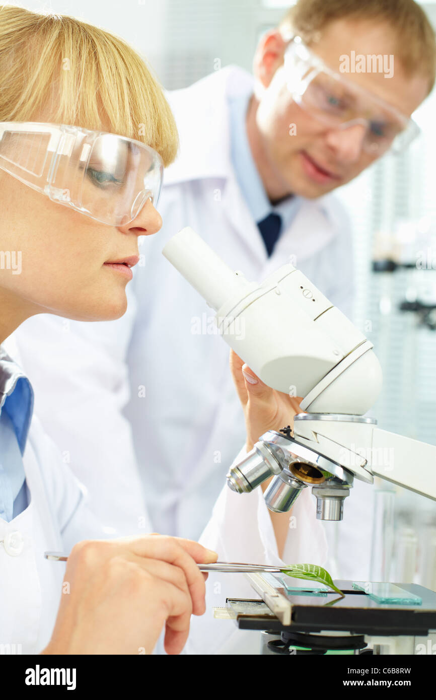 Pretty biochemist studying new substance in microscope in laboratory ...