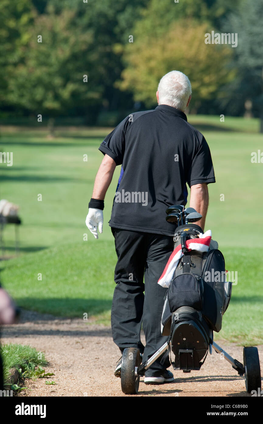 A golfer pulling his trolley with golf equipment along the path in ...