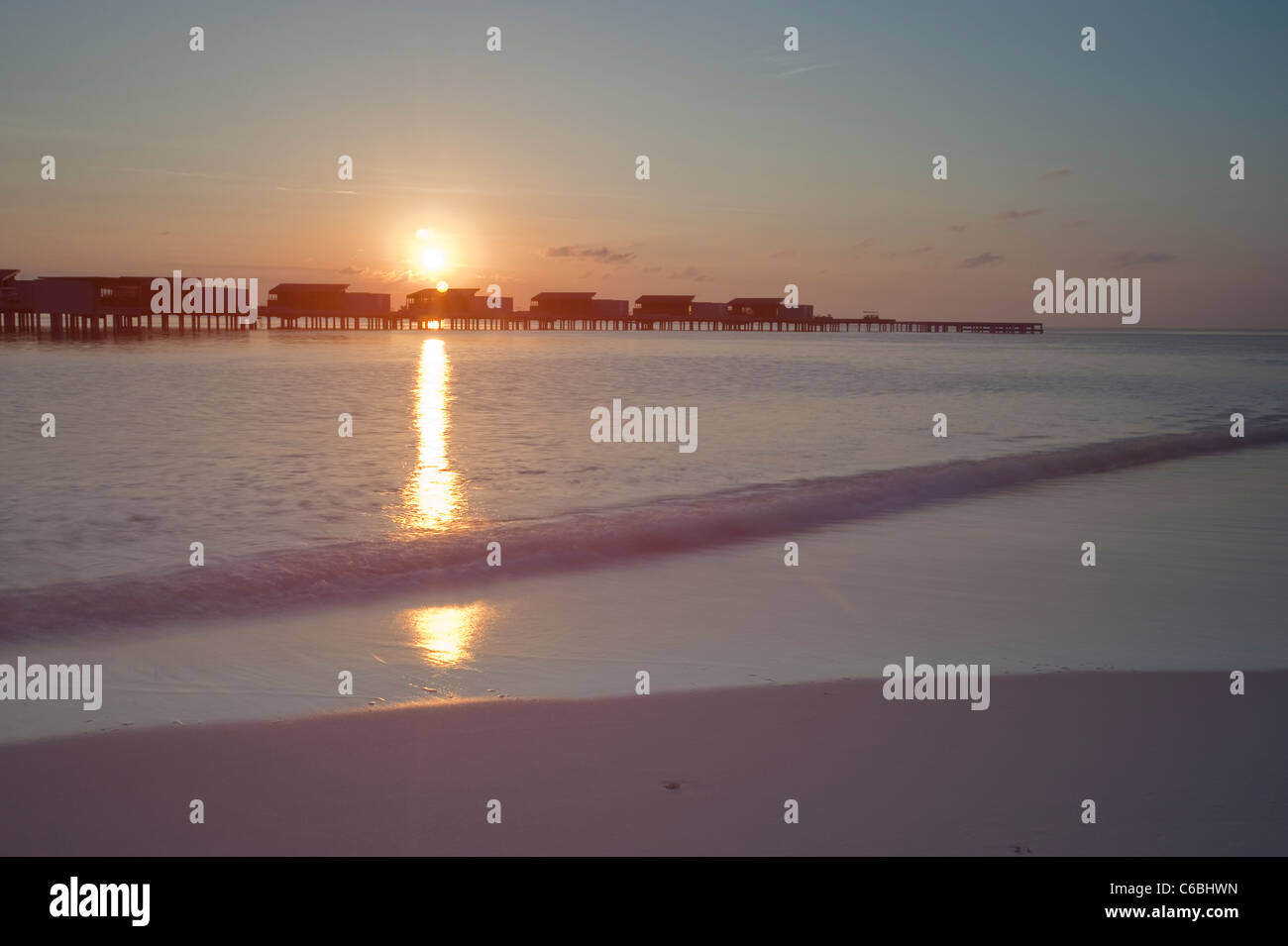 Sun setting behind water villas at the Alila Villas Hadahaa Resort ...
