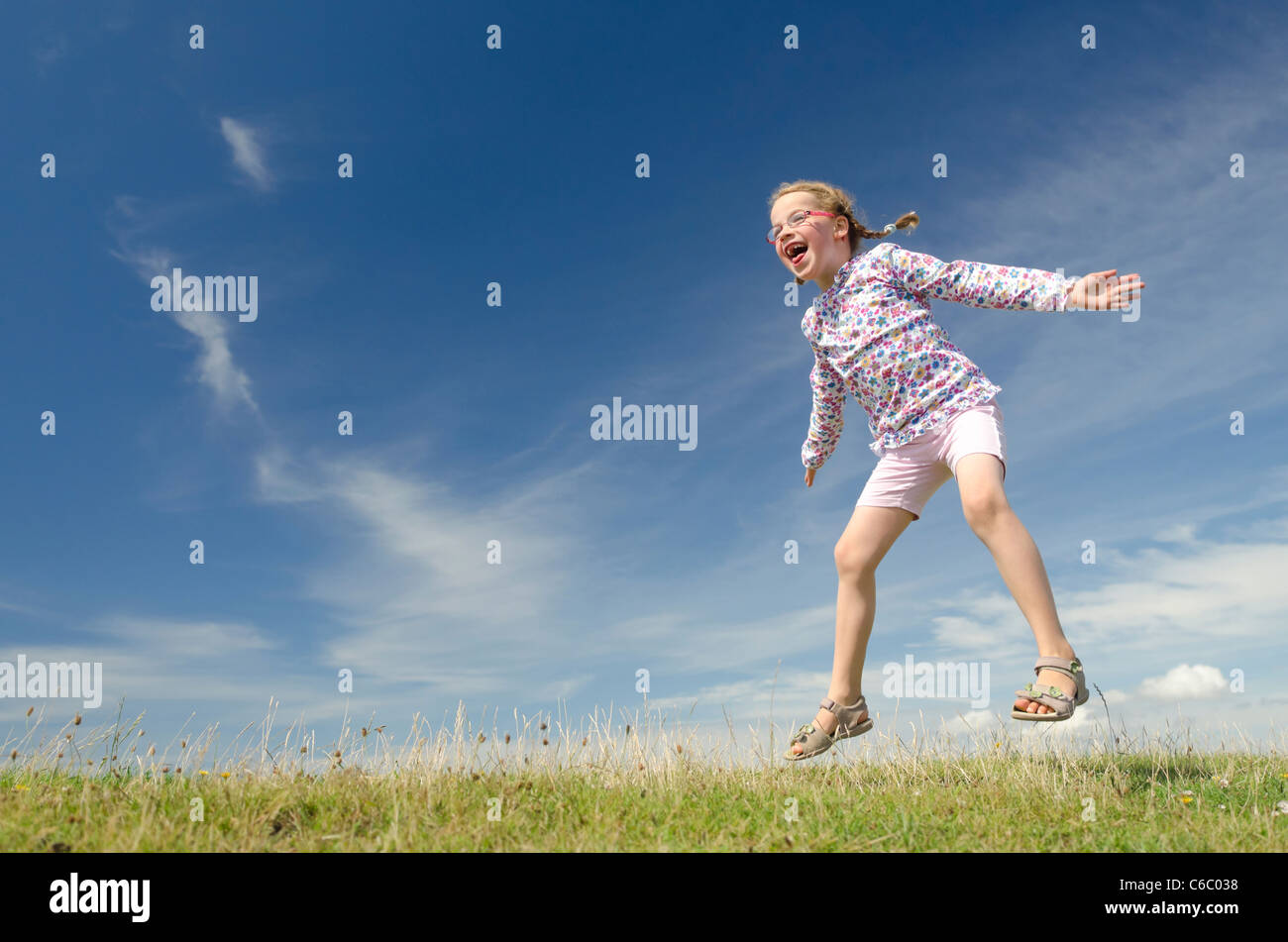 Happy little girl jumping in front of blue sky Stock Photo - Alamy