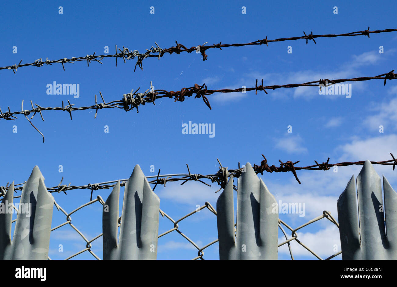Barbed wire and metal spikes form a security barrier, with blue sky ...