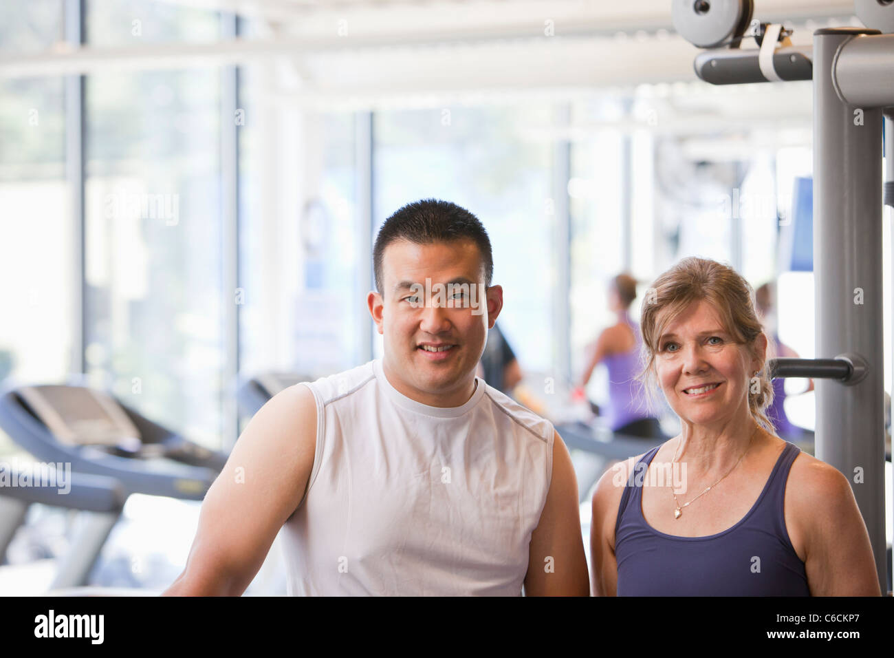 Woman standing with personal trainer in health club Stock Photo - Alamy