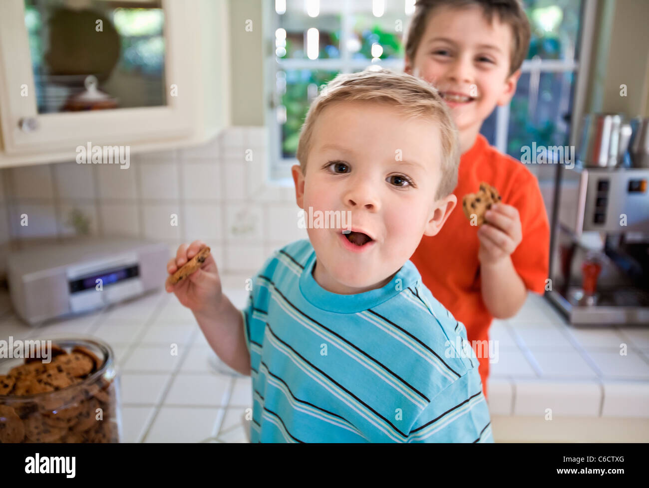 Caucasian brothers sneaking cookies in kitchen Stock Photo - Alamy