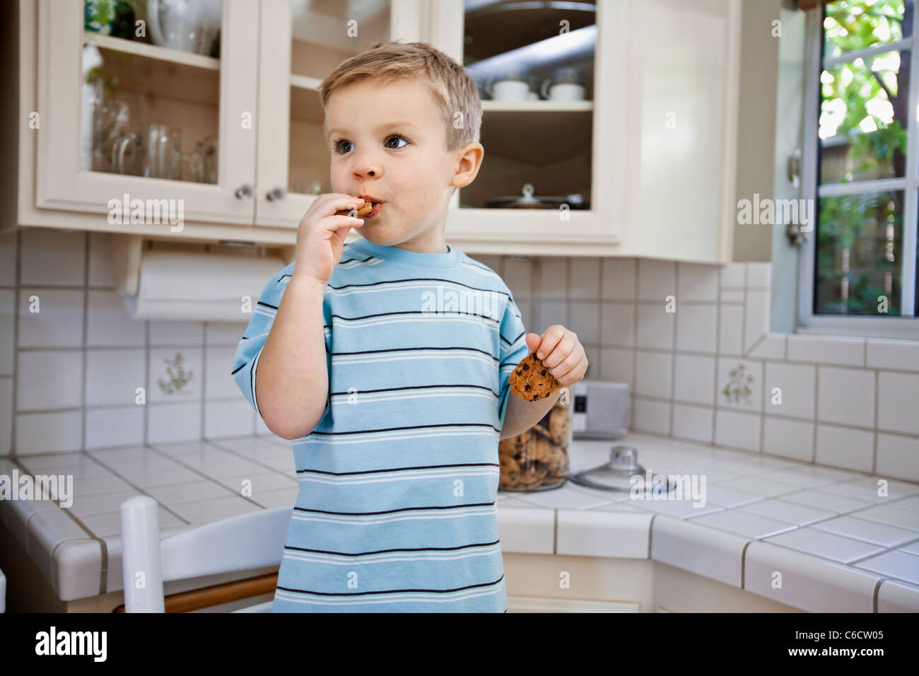 Caucasian boy eating cookie in kitchen Stock Photo - Alamy