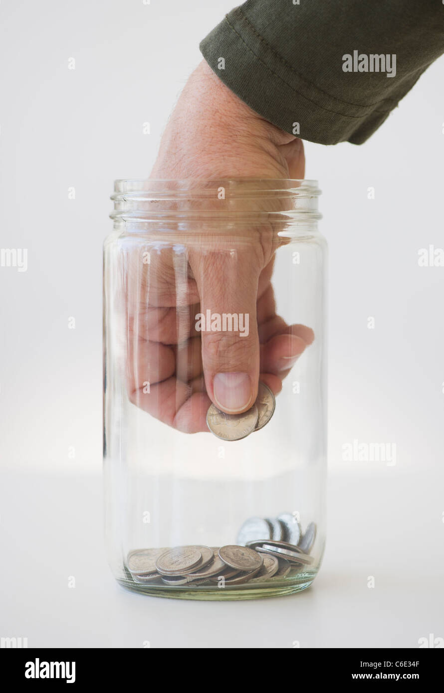 Hand inserting coin into jar Stock Photo - Alamy