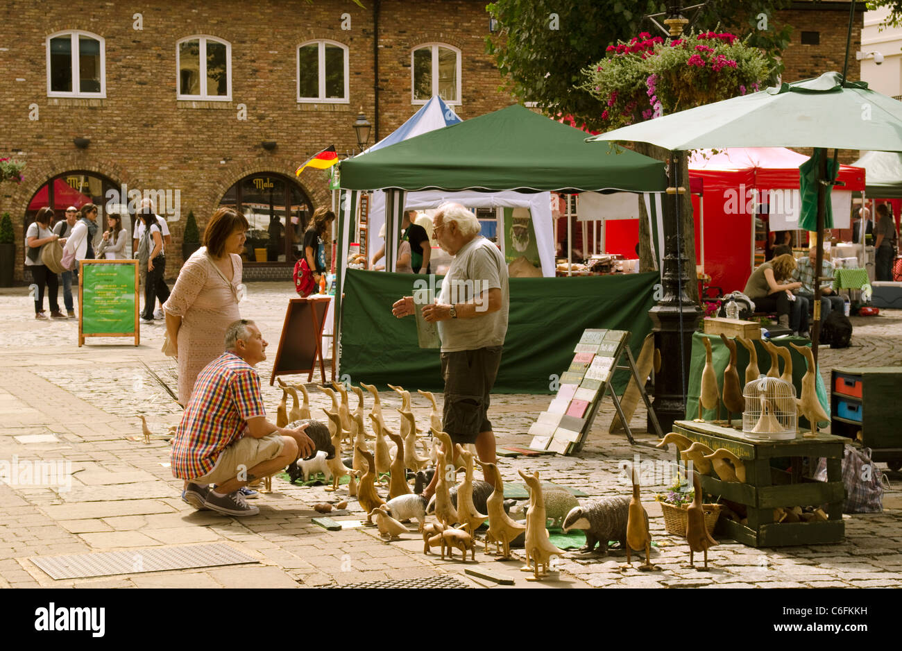 Market trader chatting to customers selling wooden ducks as garden ...