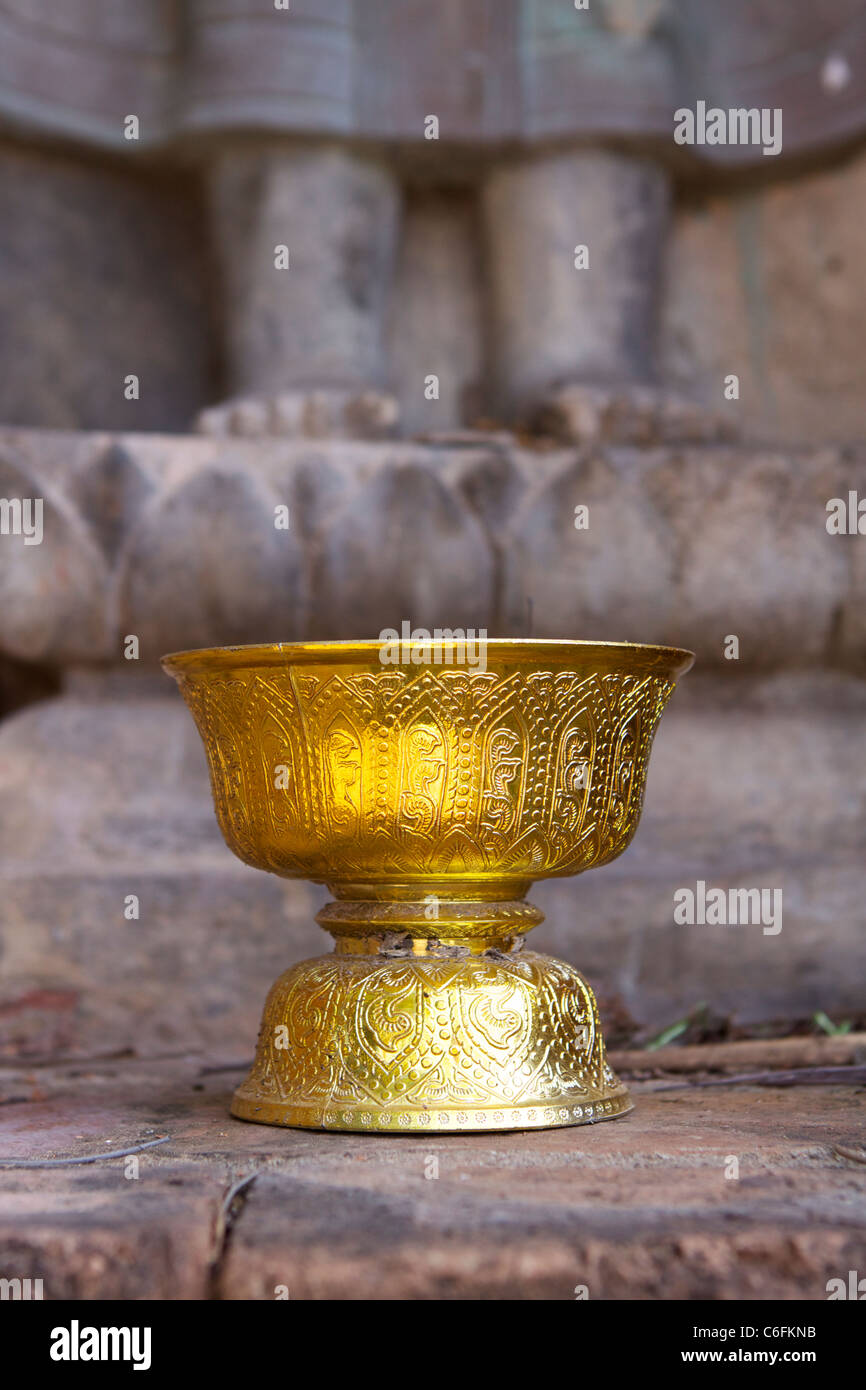 A gold coloured cup left as an offering at the feet of carved figure at ...