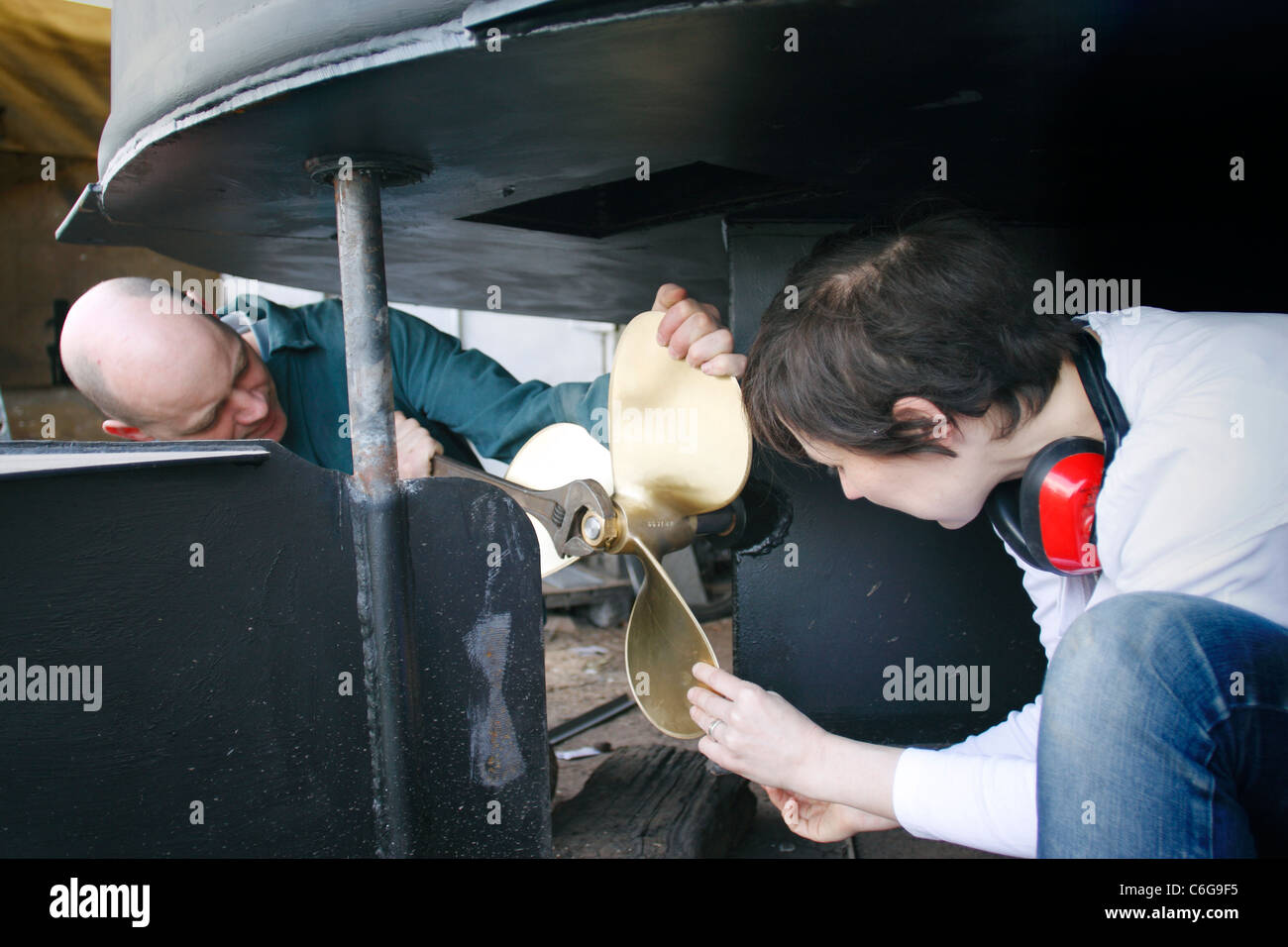 A man and a woman fixing the propeller on a narrowboat, using a spanner ...