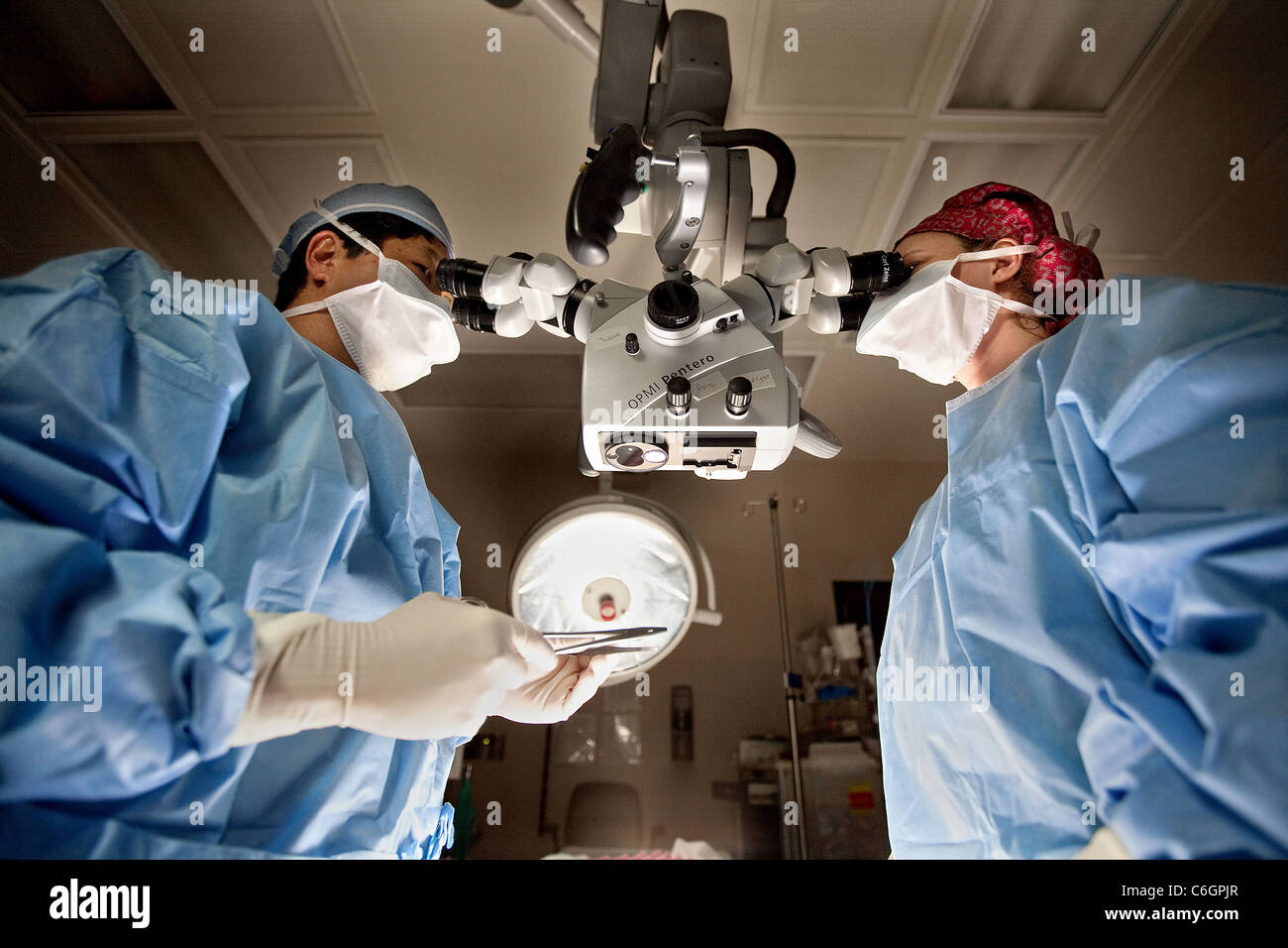 An ophthalmologist doctor works with a nurse under a microscope during ...