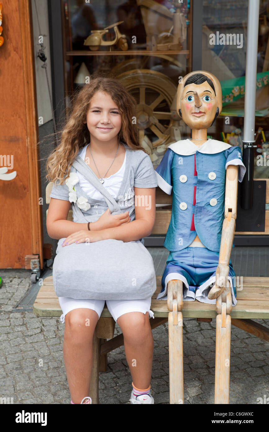 Young girl sitting on a bench by a full human size Pinocchio puppet ...