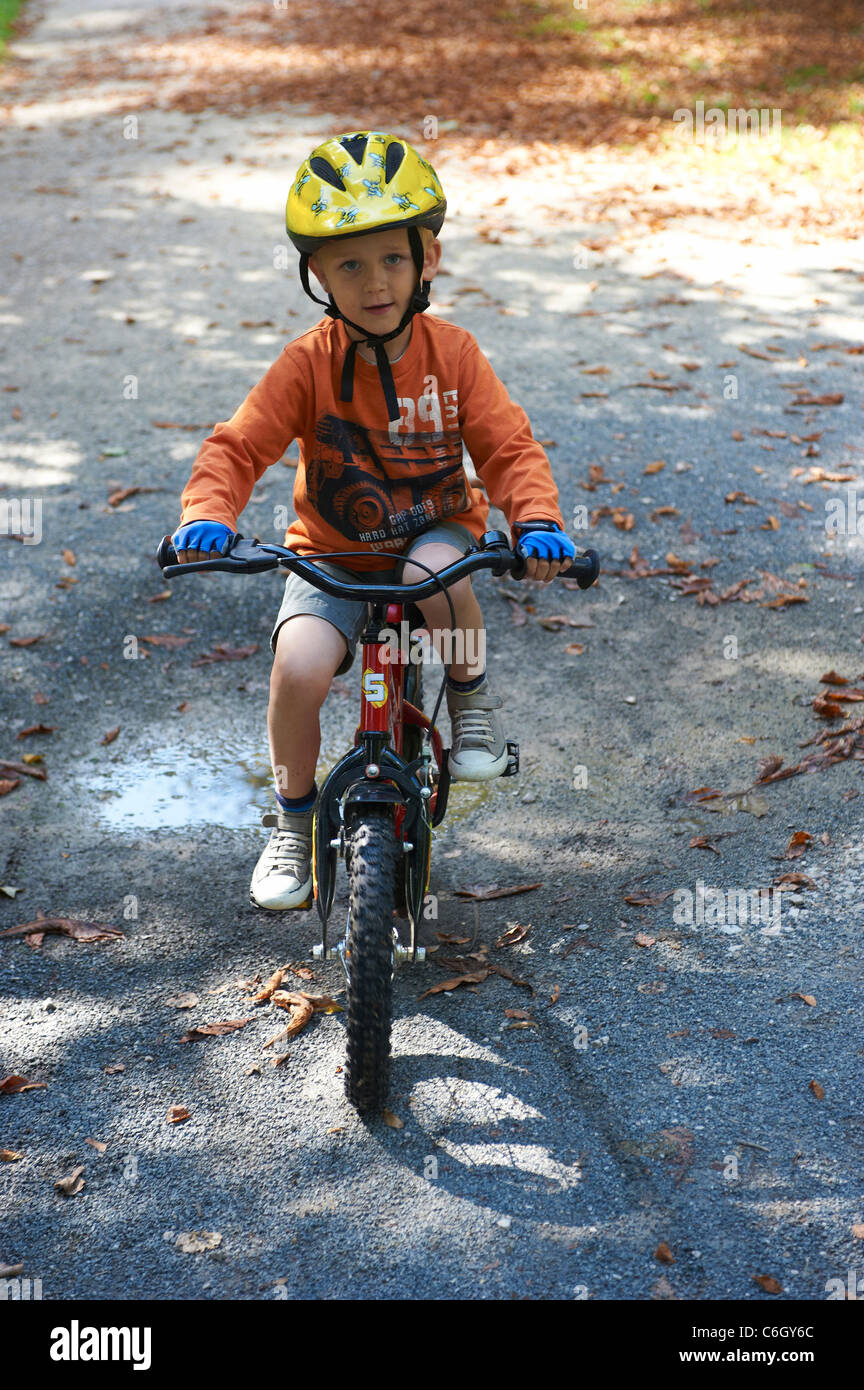 Child blond boy 5 years old riding (cycling) bicycle with safety helmet ...