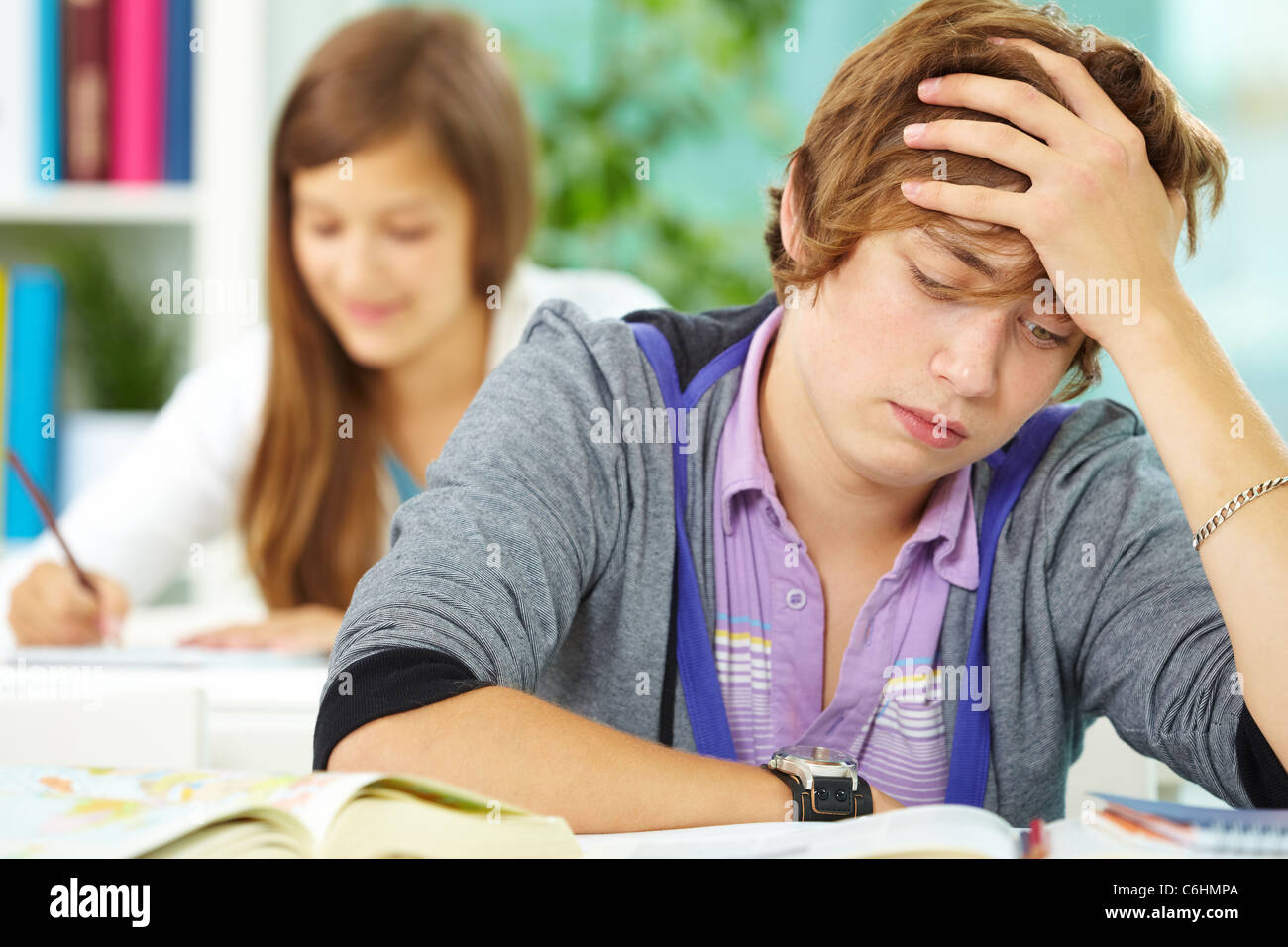Portrait of smart guy reading book in library with his classmate behind ...
