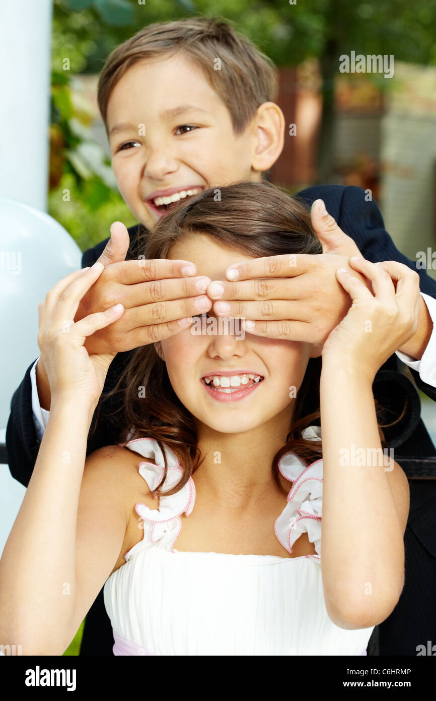 Portrait of laughing boy groom shutting eyes of his cheerful bride ...