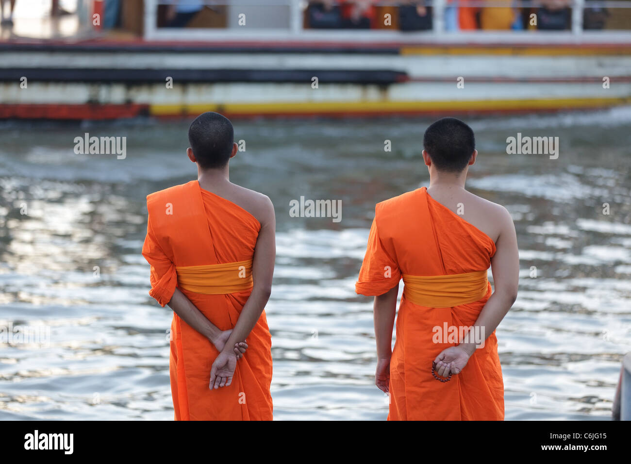 two monks standing in front of chao phraya river and passenger boat ...