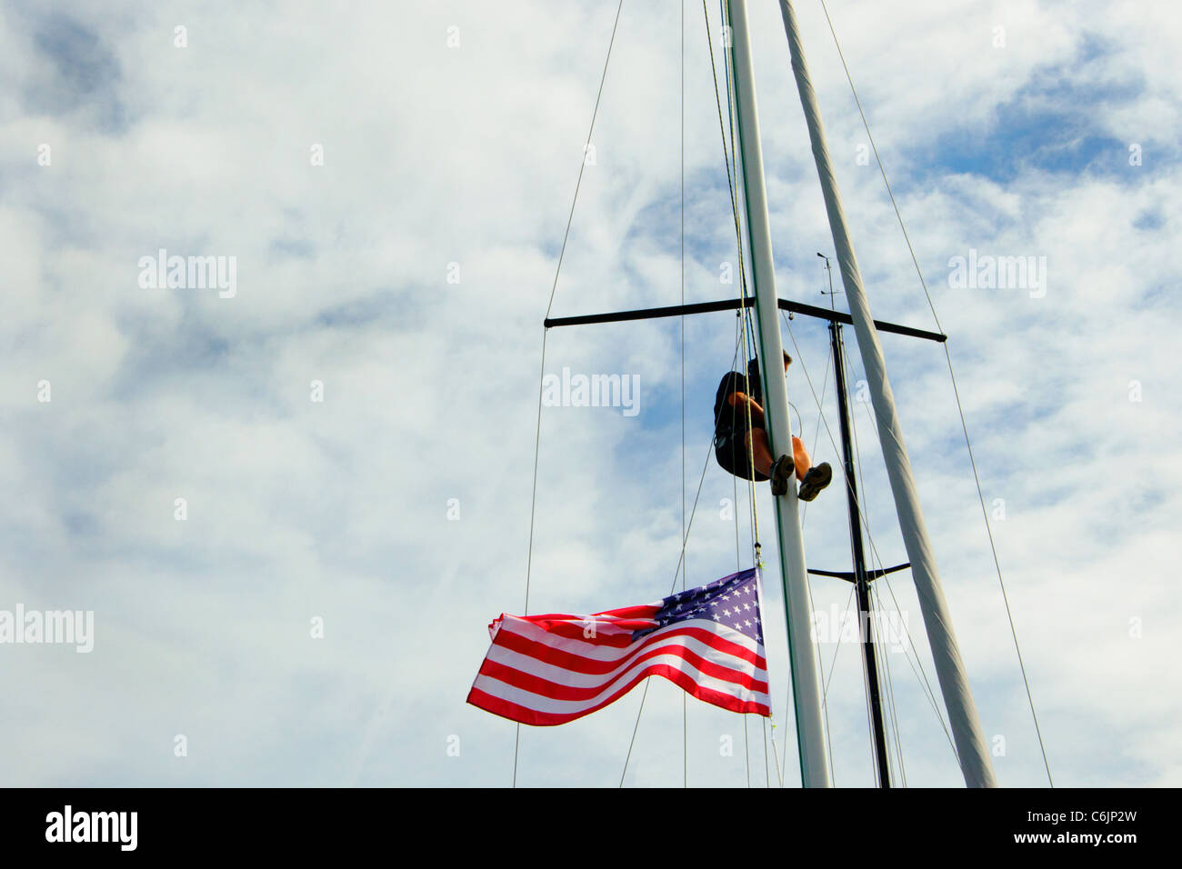 man climbing yacht mast with stars and stripes flag flying with the sky ...
