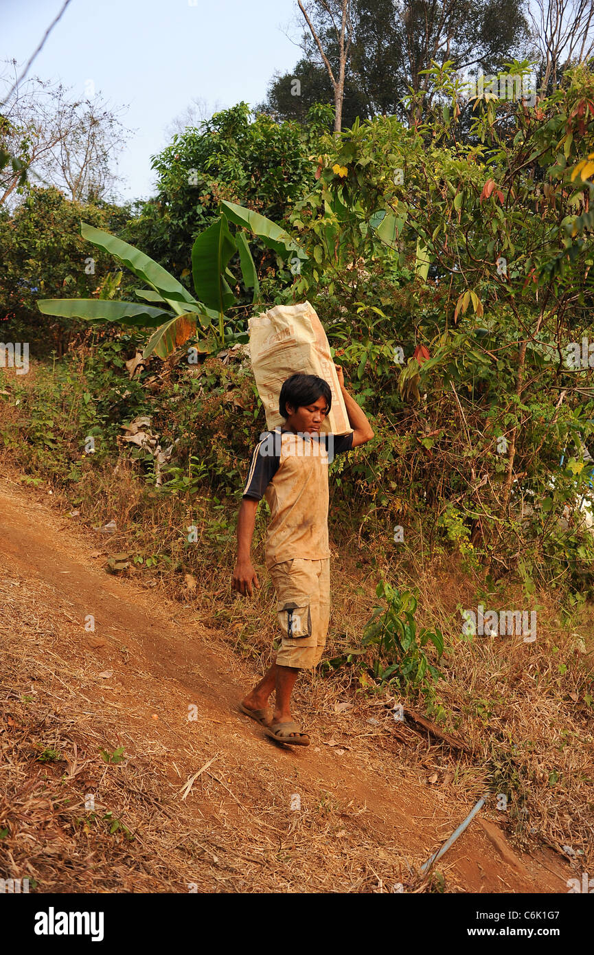 Young adult carrying heavy sack of building material down steep slope ...