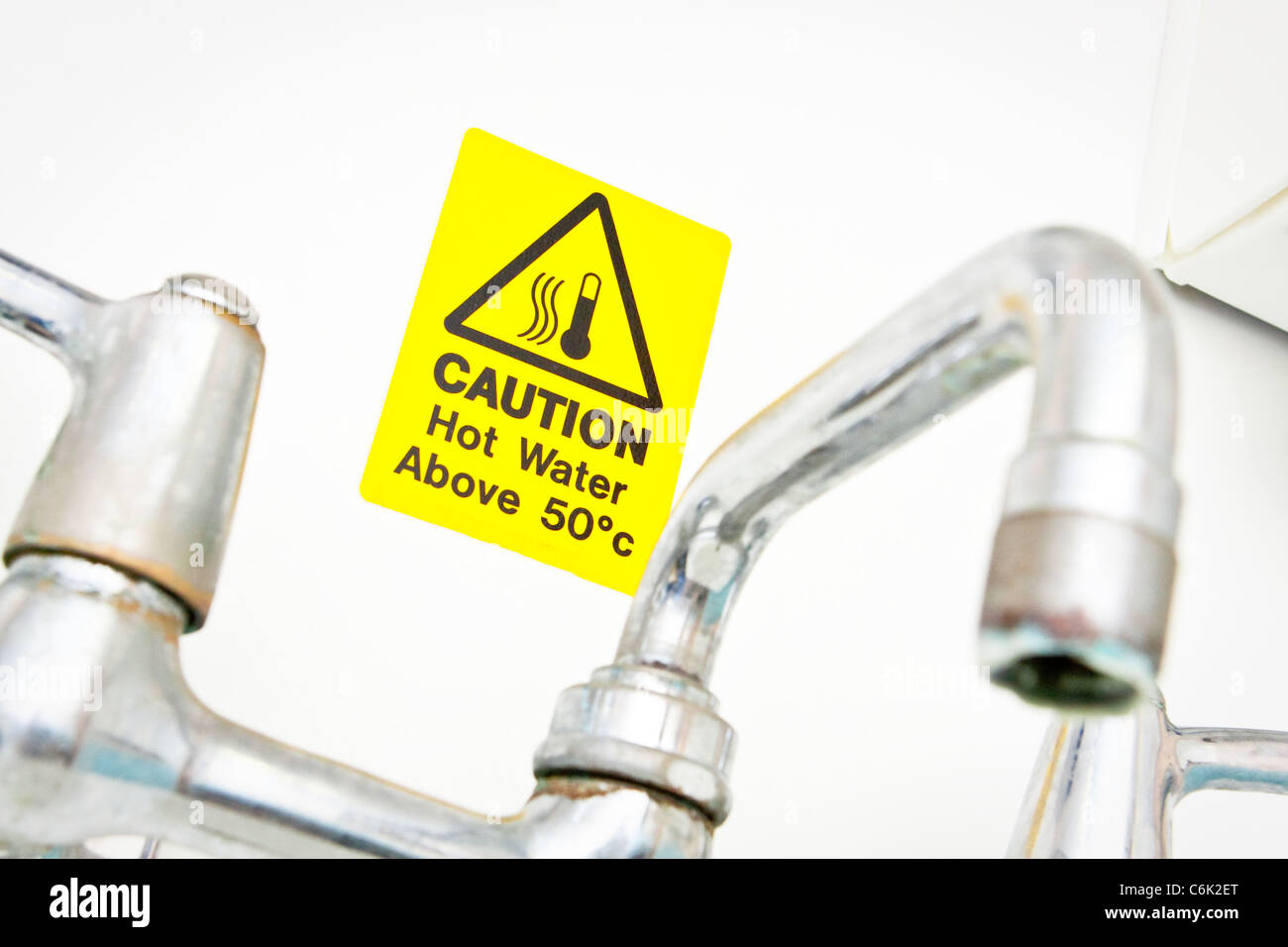 A bright yellow hot water warning notice behind a chrome tap Stock ...