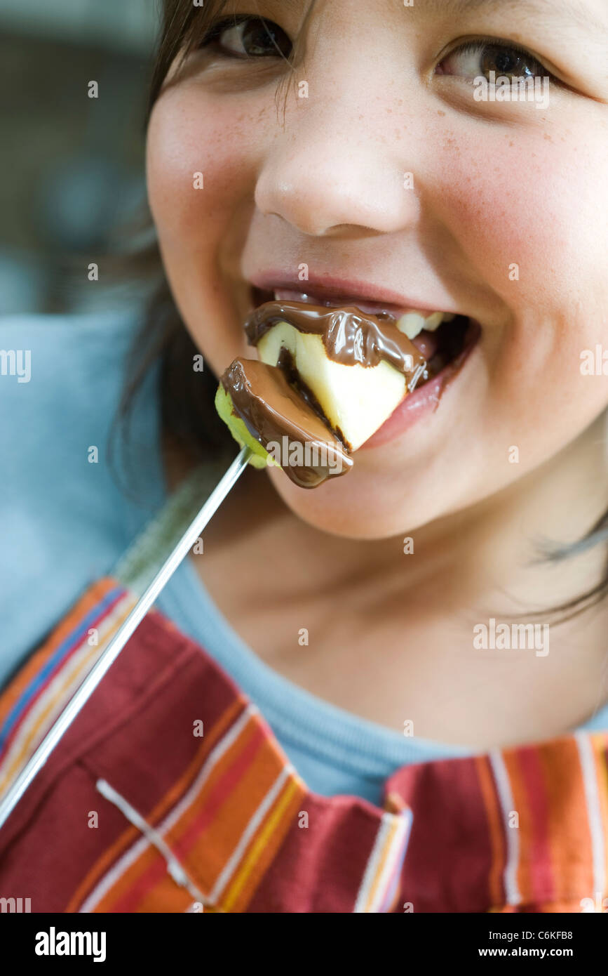 Girl eating apple chunk dipped in chocolate fondue Stock Photo - Alamy