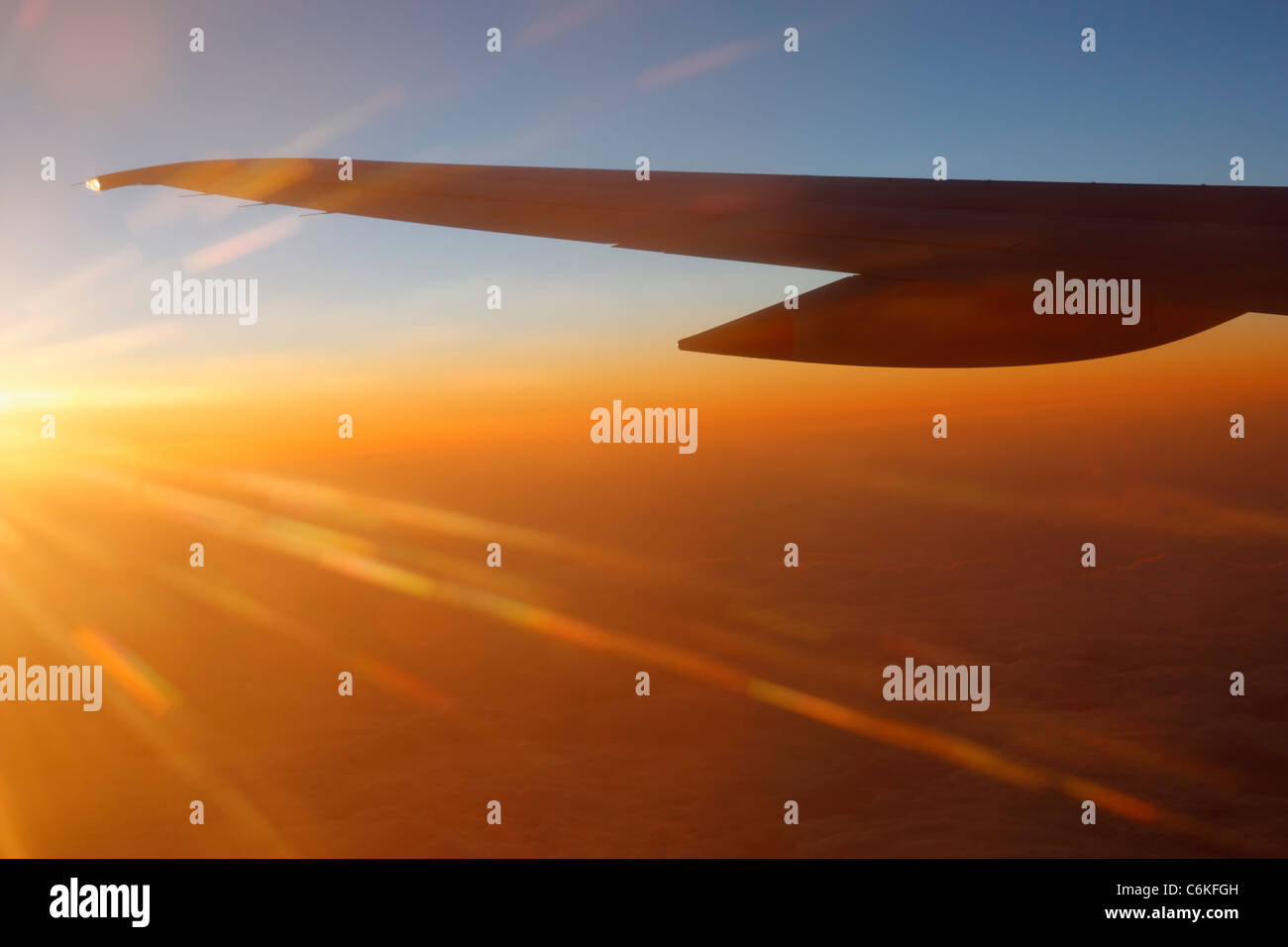 View from window seat of airplane wing over layer of cloud at sunset ...