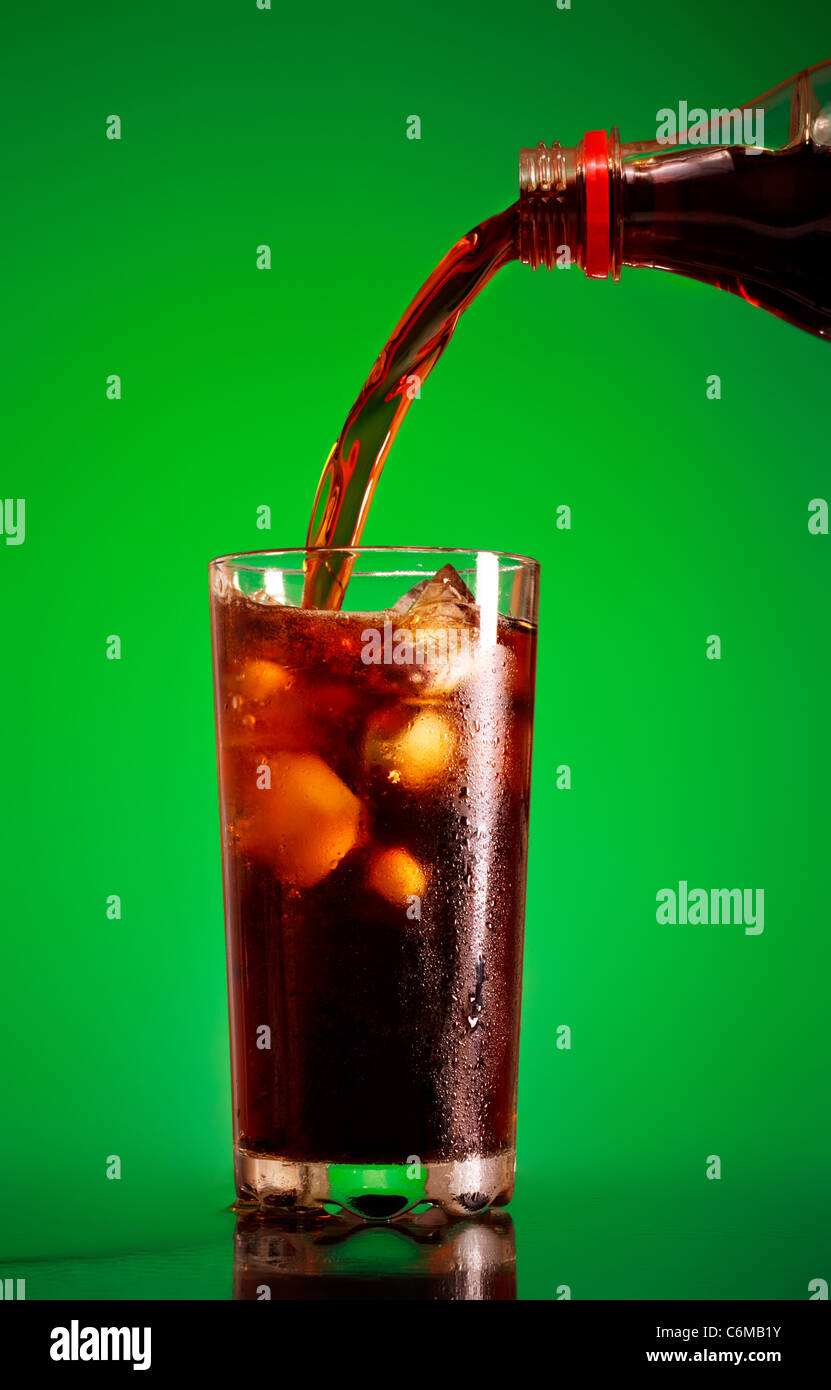 pouring cola in glass over green background Stock Photo - Alamy