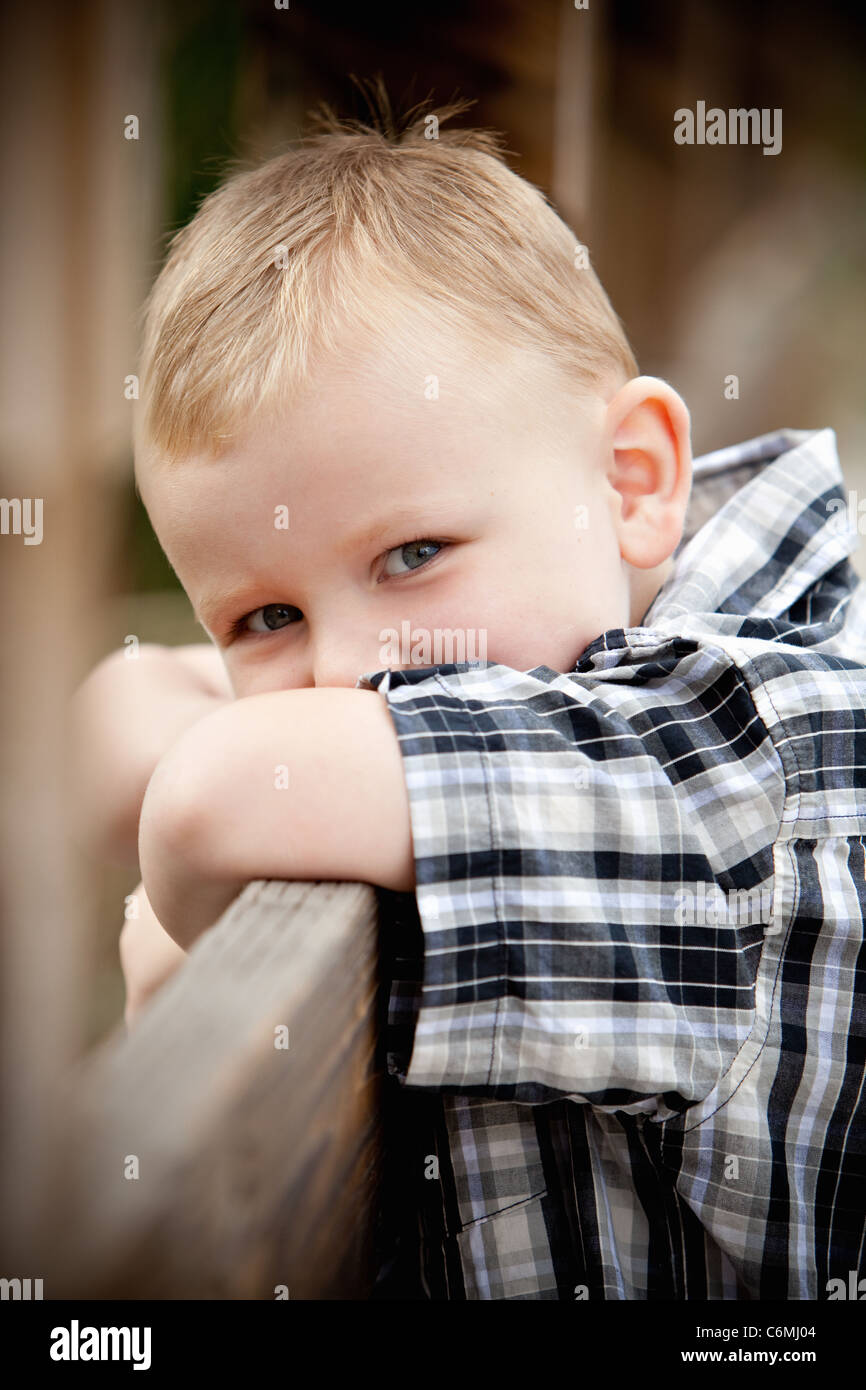 Young boy sneaking a glance leaning on a fence Stock Photo - Alamy
