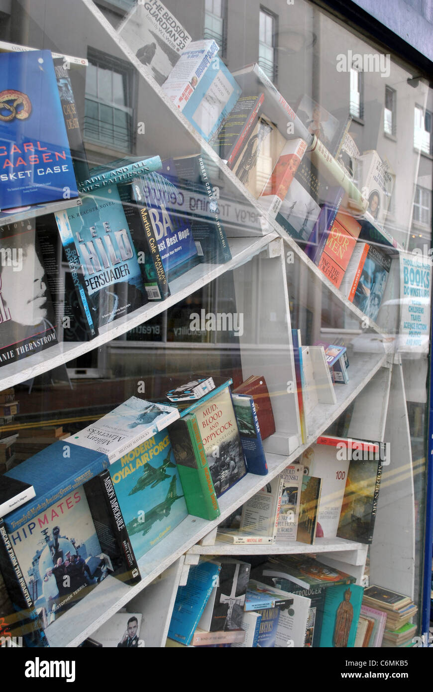 Books on angled bookshelves with reflection of houses on shop window ...