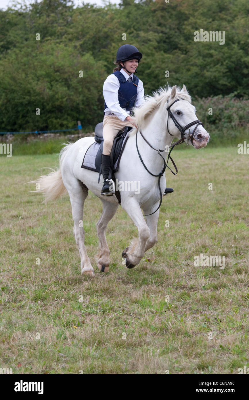 Smiling teenage girl rider cantering on white horse North Cotswold Pony ...