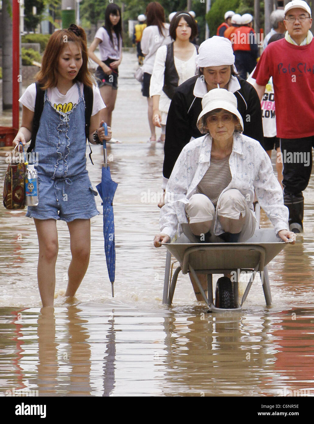 A woman is carried on a wheelbarrow on a flooded road in Sanyo-Onoda ...