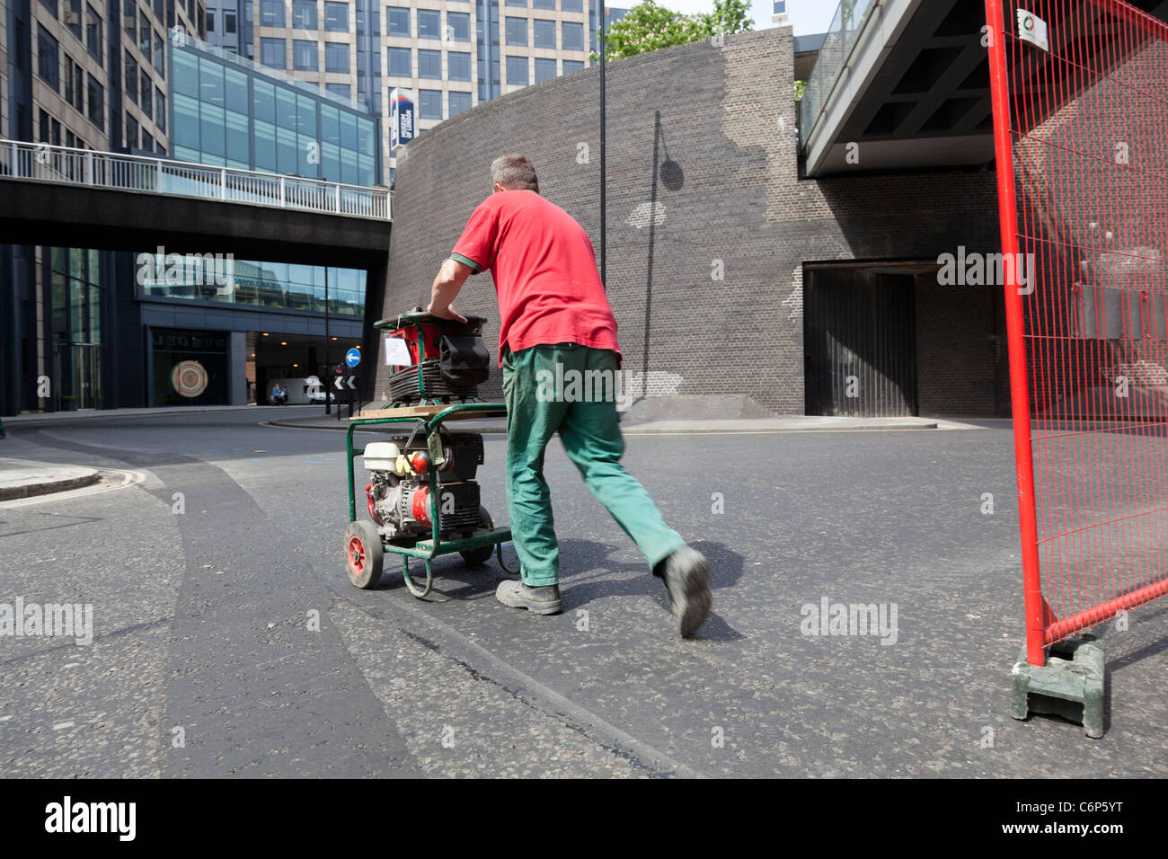 Workman crosses the road with compressor equipment on a trolley, London ...