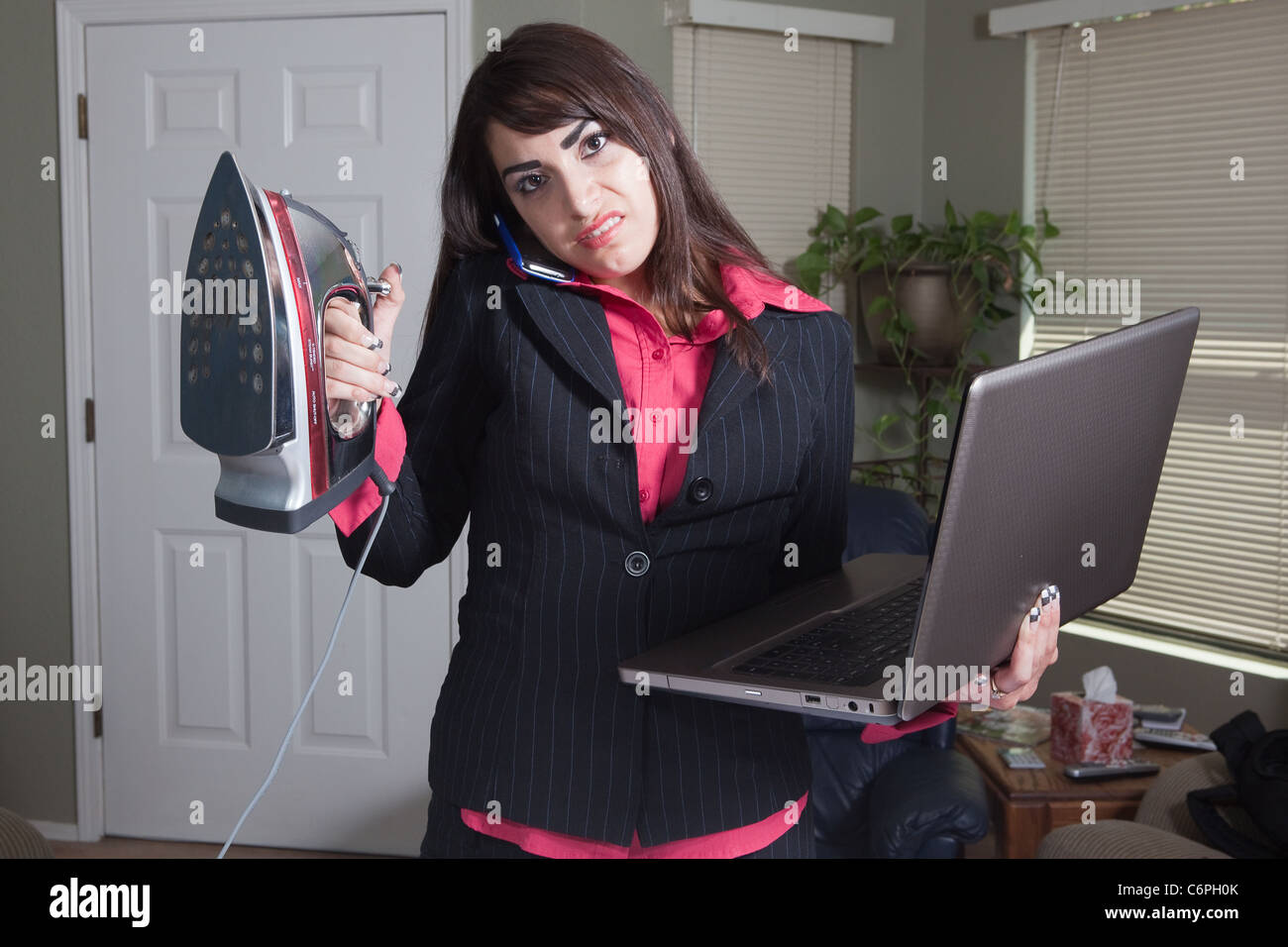 Angry woman handling a business call while trying to iron and work on ...