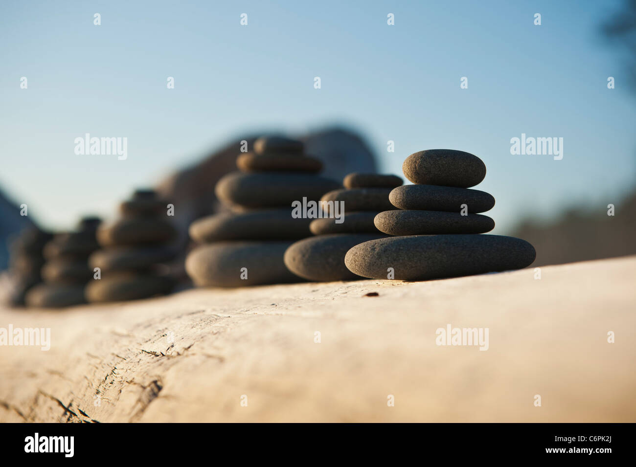 Rock piles on log at beach Stock Photo - Alamy