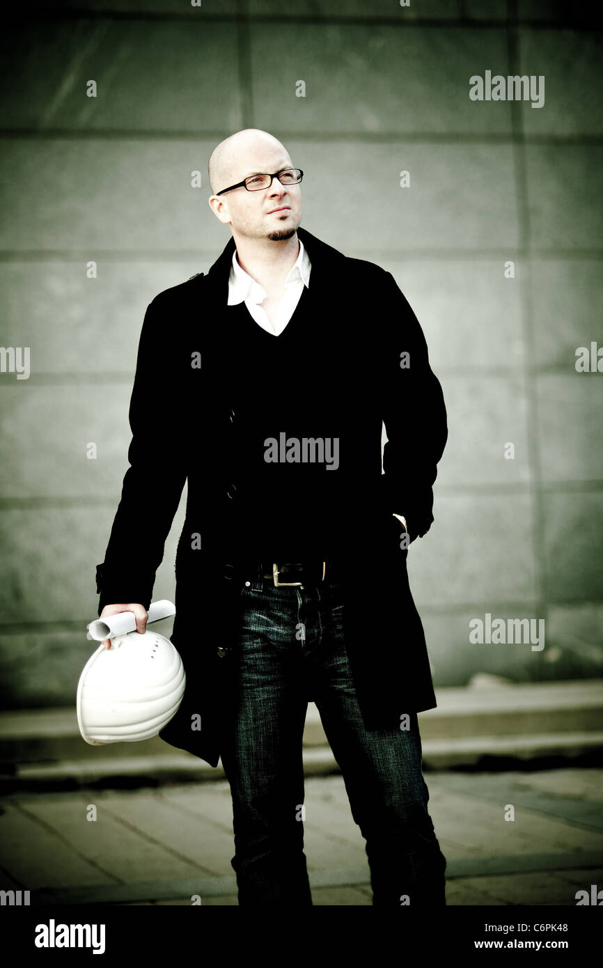 Architect with helmet and plan in front of a modern facade, cold shades ...