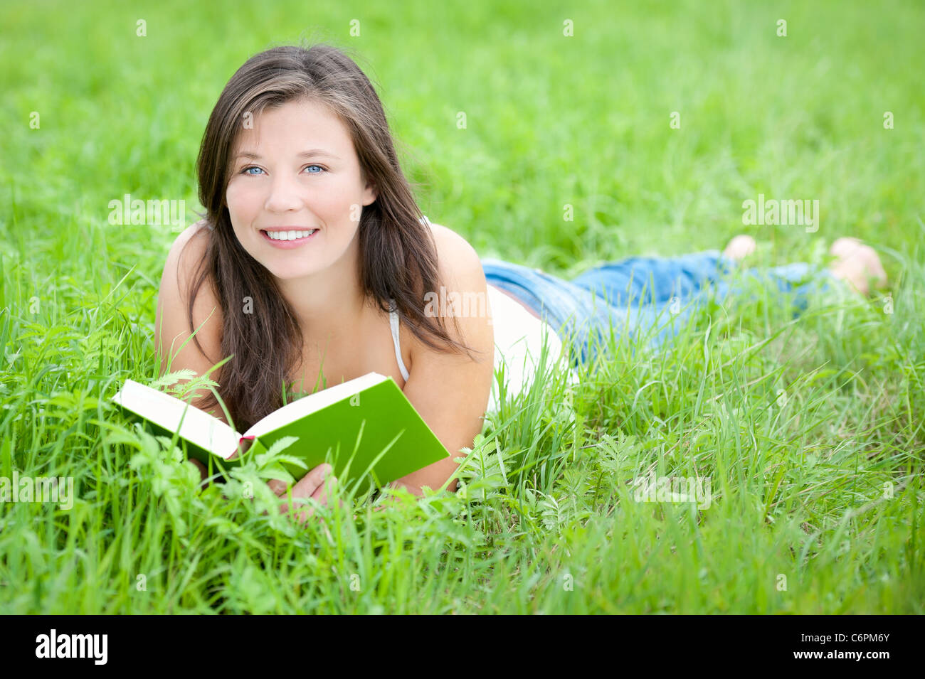 Outdoor portrait of a cute teen reading a book while lying in green ...