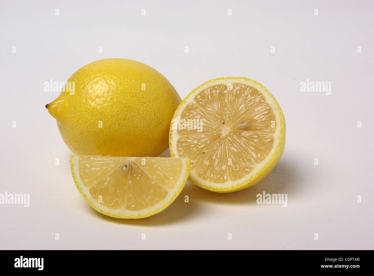 A whole lemon sits on a white background alongside of a quarter of a ...